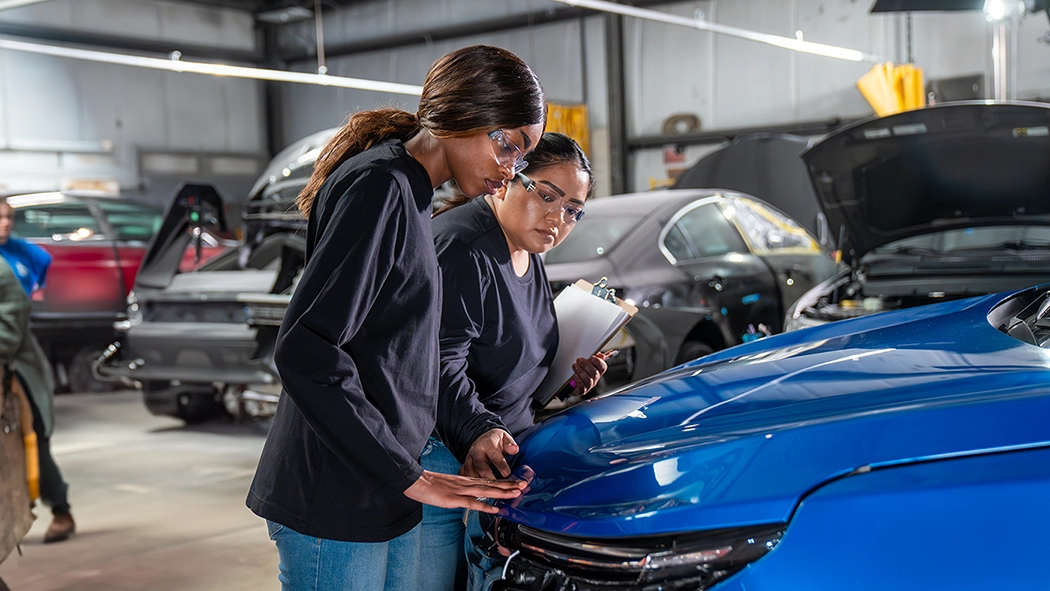 Two female collision repair technicians examining a car in an auto ...