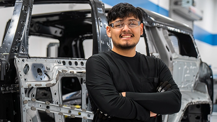 A collision repair technician standing in front of a vehicle in a workshop.