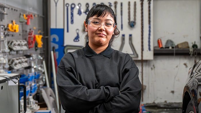 A female collision repair technician standing in a garage with her arms ...